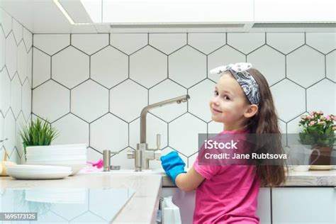 분홍색 티셔츠를 입고 큰 파란색 고무 장갑을 끼고 싱크대 근처에 서 있는 긴 검은 머리를 가진 어린 초반 소녀의 뒷모습 4 5세에 대한 스톡 사진 및 기타 이미지 Istock