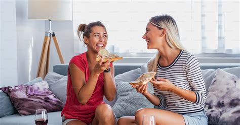 집에서 소파에서 와인과 함께 피자를 먹는 행복한 젊은 여자 친구들 행복한 미소를 짓는 젊은 여성 친구들은 피자를 먹고 집에서 와인 부틀을 엽니다 사진 Unsplash