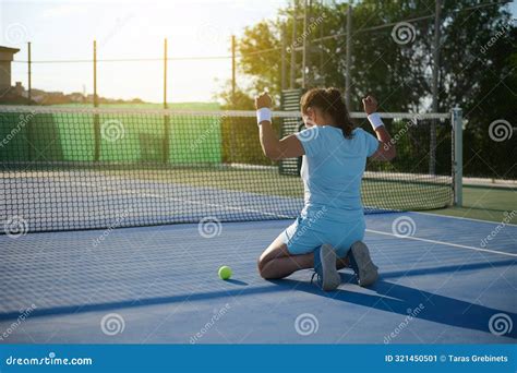 Woman Celebrating Victory On Tennis Court Kneeling With Raised Fists