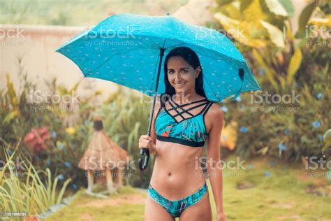 수영복을 입고 수영복을 입고 포즈를 취하고 우산 아래에 서있는 아름다운 무두질 한 여성 백그라운드에서 식물 열대 리조트에서휴가의 개념 가냘픈에 대한 스톡 사진 및 기타