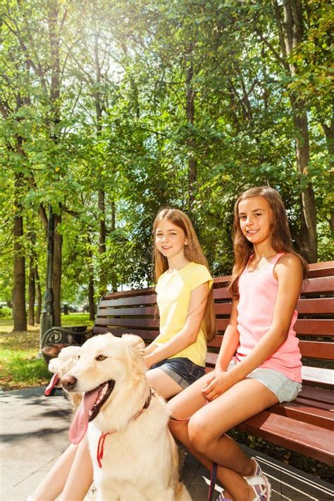 2 счастливых девушки сидя на стенде в парке Стоковое Изображение изображение насчитывающей