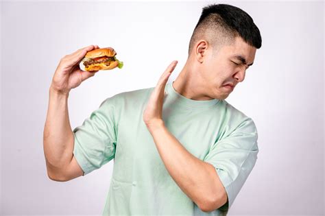 민트색 셔츠를 입은 아시아계 남성이 치즈버거가 담긴 접시를 들고 다른 손을 뻗어 멈춰 서려는 제스처를 취하고 있다 그는 놀랐거나 못마땅한 표정을 지었다 배경은 일반