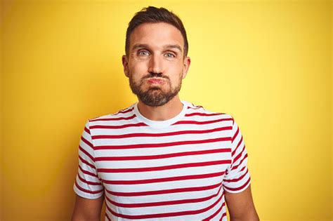 젊은 잘 생긴 남자 캐주얼 빨간 줄무늬 티셔츠 위에 노란색 고립 된 배경 퍼핑 뺨 재미 있는 얼굴 공기 미친 표정으로 입이 팽창 공기 주입에 대한 스톡 사진 및 기타 이미지