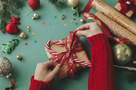 즐거운 성탄절 녹색 배경에 세련된 크리스마스 선물 황금 포장지 빨간 리본 및 축제 장식을 감싸는 손 포장 크리스마스 선물 개념 즐거운 휴일 보내세요 12월에 대한 스톡 사진