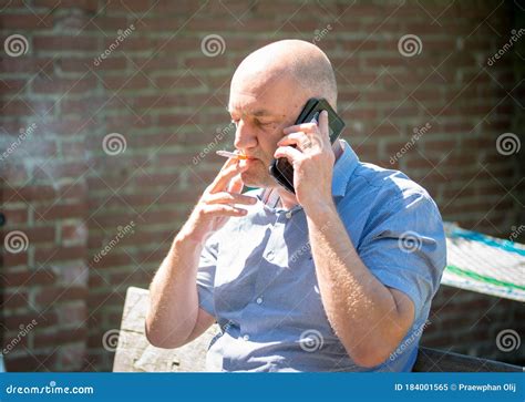 Een Man Aan De Telefoon Terwijl Hij Een Sigaret Rookt Stock Afbeelding