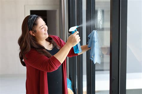 쾌활하고 행복한 아시아 여성은 헝겊과 스프레이 세제로 창문 유리 표면을 씻거나 청소하는 동안 웃고 있다 집 청소 작업 개념을 하는 주부 가사 집안일에 대한 스톡 사진 및