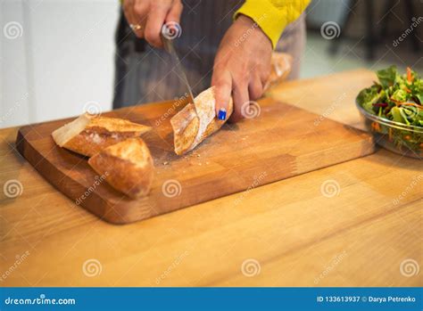Cropped Shot Of Woman Cutting Baguette Bread On The Tabletop Stock