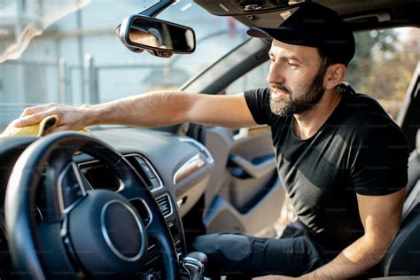 검은색 티셔츠를 입은 잘 생긴 세탁기와 노란색 극세사가 있는 고급 자동차 인테리어의 패널을 닦는 모자 사진 Unsplash의