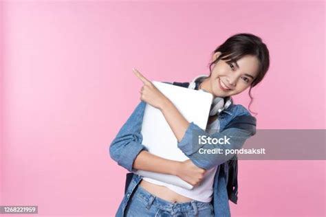 젊은 행복 아시아 여자 들고 노트북 가리키는 손가락 손을 복사 공간 그녀는 청바지 재킷을 입고 분홍색 배경에 고립 된 배낭 셔츠
