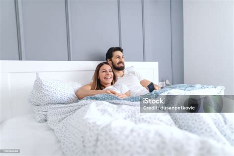 젊은 웃는 행복 한 매력적인 백인 커플 침대에 누워 아침에 텔레비전을 보고 침실 인테리어입니다 가정 생활에 대한 스톡 사진 및