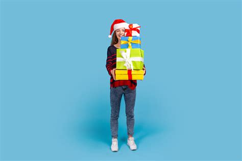 스웨터와 산타 클로스 모자를 쓰고 선물 상자를 들고 크리스마스와 새해 전야인사와 함께 물결 치는 머리를 한 행복한 여성의 전체 길이 초상화 전신에 대한 스톡 사진 및 기타