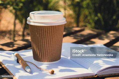 나무 벤치에 빈 종이 노트북이 있는 크래프트 종이에 커피 또는 차가 있는 에코 재활용 종이컵 야외에서 일하는 연구의 개념 커피를