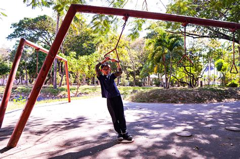 이미지는 공공 피트니스 공원에서 허리와 팔 근육을 훈련하기 위해 삼각형 금속 손잡이를 사용하여 원형 스윙 운동을 시연하는 어린 소년을 보여줍니다 10 11세에 대한 스톡