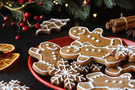 진저 브레드 남자와 화이트 로얄 아이싱 스타 아니스 계피 스틱 묶음 말린 감귤류 오렌지 과일 조각 가문비 나무 바늘과 붉은 열매 검은 배경에 조명 요정 조명과 진저 브레드