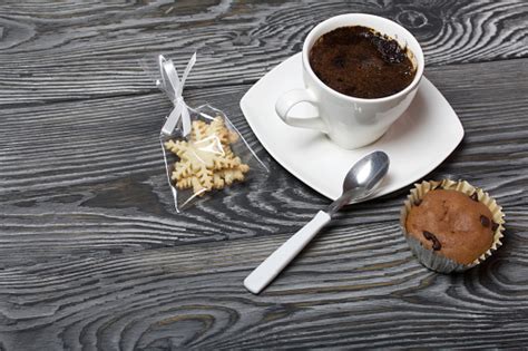 흰 컵에 커피가 접시 위에 서 있습니다 근처에는 머핀과 접시에 숟가락이 놓여 있습니다 가방에 눈송이의 형태로 쿠키 세트 기모 소나무 보드에 검은색에 대한 스톡 사진 및 기타