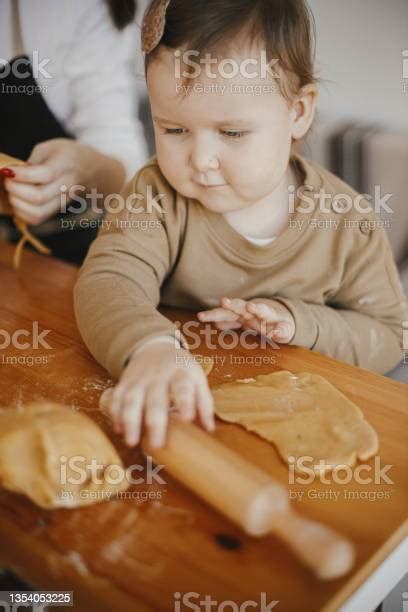 사랑스러운 아기 딸이 현대 스칸디나비아 방에있는 나무 테이블에 진저 브레드 쿠키에 대한 어머니와 함께 반죽을 반죽 귀여운 유아 소녀는 크리스마스 쿠키를 만드는 데 도움