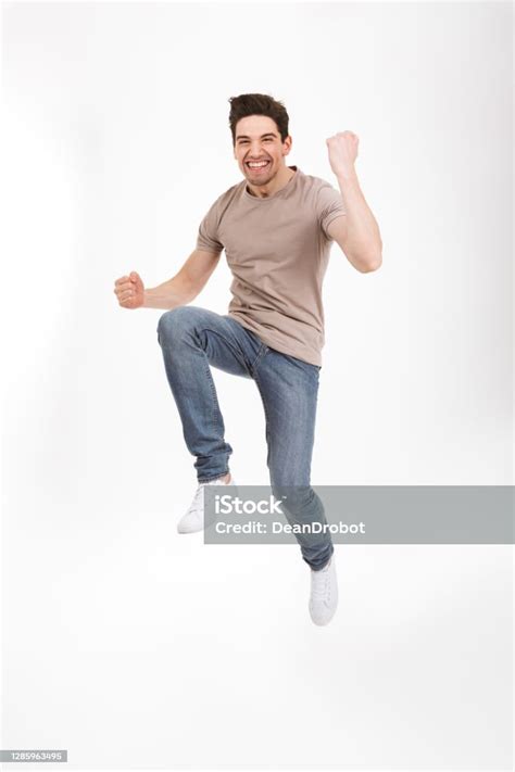 흰색 배경에 고립 된 주먹을 움켜 쥐고 있는 동안 캐주얼 한 티셔츠와 청바지를 입은 흥분 한 남자 30 대 의 전체 길이 사진