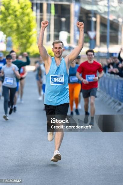 낮에 도시 마라톤에서 결승선을 통과하는 운동 선수 청년 가족과 친구들이 관중석에서 그를 응원하는 가운데 축하하는 회복력 있는 우승 주자 마라톤에 대한 스톡 사진 및 기타