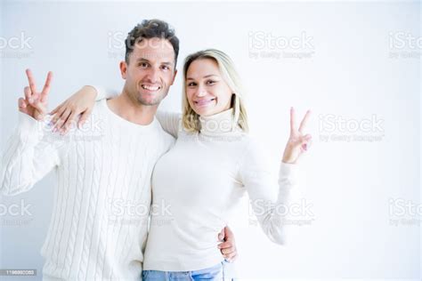 고립 된 흰색 배경 위에 서있는 캐주얼 한 티셔츠를 입은 젊은 아름다운 부부는 승리의 표지판을하고있는 카메라에서 행복한 얼굴