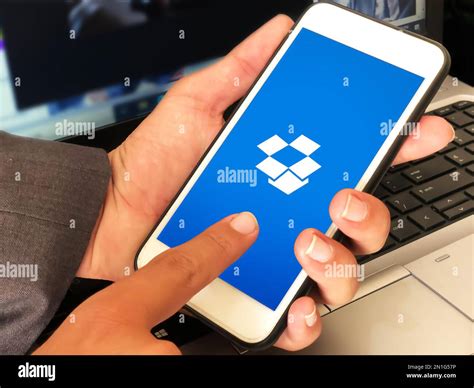 Man Using Storage Application Dropbox On Mobile With Laptop In The Backdrop Editorial Tech