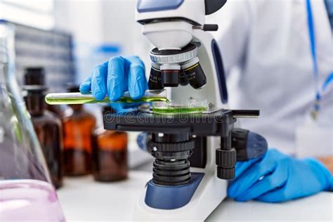 Young Blond Man Scientist Using Microscope Pouring Liquid On Sample At