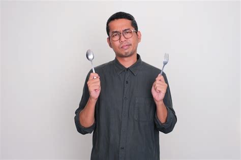 Premium Photo Adult Asian Man Showing Confuse Expression While Holding A Spoon And Fork