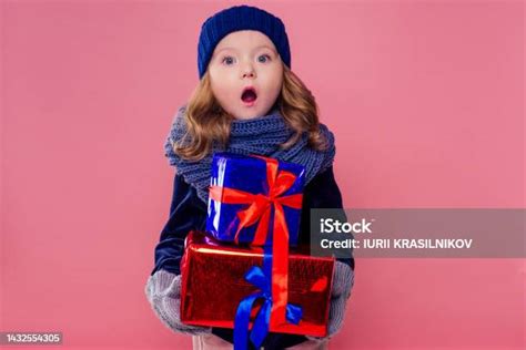 작은 금발 곱슬 머리 스타일 소녀 니트 핑크 모자 스카프와 선물 크리스마스 박스 핑크 배경 스튜디오의 벙어리 산 소원 카피 스페이스를 만드는 여성 어린이의 손에 새해가