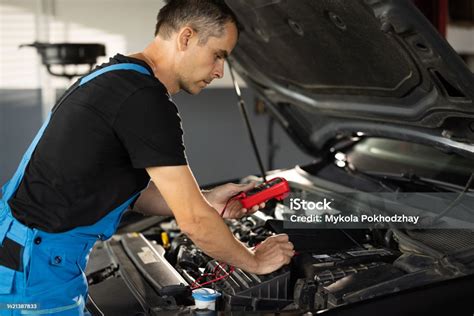 전문 자동차 정비사는 전기 멀티 미터로 배터리 전압을 확인합니다 자동차 진단 자동차 정비사 수리공은 차량 서비스 워크샵에서 진단 장비에 엔진 고장을 찾습니다 35 39세에