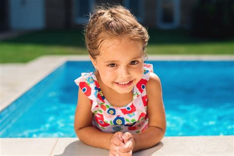 Menina Sorridente Segurando Na Beira Da Piscina E Olhando Para A Câmera