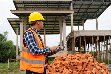 안전모를 쓰고 안전조끼를 입은 남성 건축가가 현장에서 건축 문서를 검토하고 있다 주택 구조 철제 골조 벽돌 및 지붕 설계에 중점을 둔 건설 계약자 40 44세에 대한 스톡