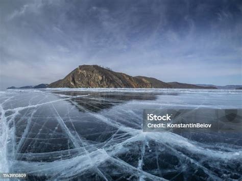 눈과 호 아 르 서 리로 덮인 돌이 있는 얼어 붙은 섬 근처의 바이칼 호수의 균열과 균열이 있는 투명 한 얼음 부드러운 미 끄 러운 표면은 구름과 하늘 아래 반사와 유리