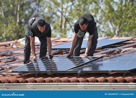 Workers Installing Alternative Energy Photovoltaic Solar Panels On Roof