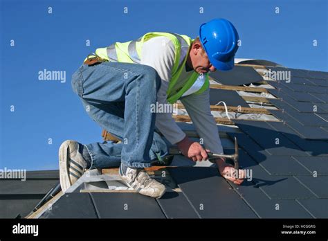 A Roofer Nails Slates Over Timber Battens And Roofing Felt On A New