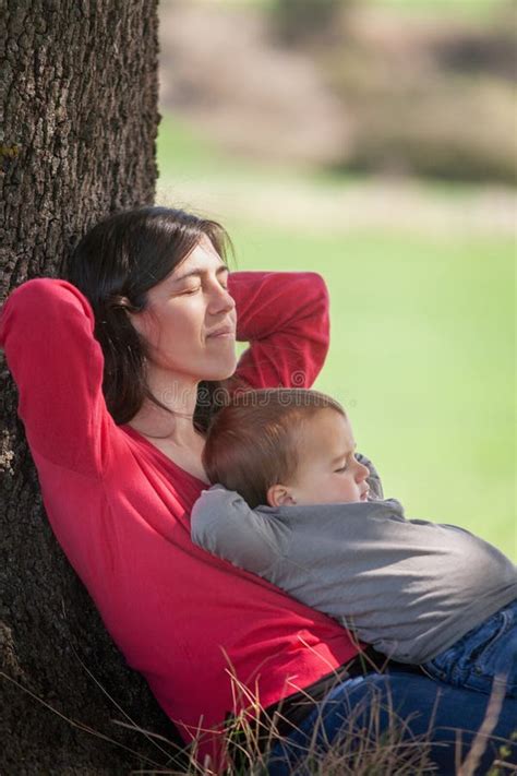 Mother And Son Sleep In The Shade Of A Tree Leaning Against The Trunk