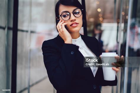 테이크 아웃 컵을 들고 야외에서 커피 휴식 중에 전화로 이야기하는 심각한 기업 관리자 동료와 모바일 대화를 하는 휴식을 즐기는 정장 웨어와 안경에 사업가 갈색 머리에 대한