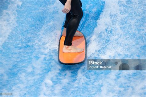 가짜 파도에 오렌지 서핑 보드에 균형 검은 수영복을 입고 워터 파크의 해변 파도 시뮬레이터 매력에서 서핑 여자 야외 수상 스포츠 활동 서핑 수상 스포츠에 대한 스톡 사진 및