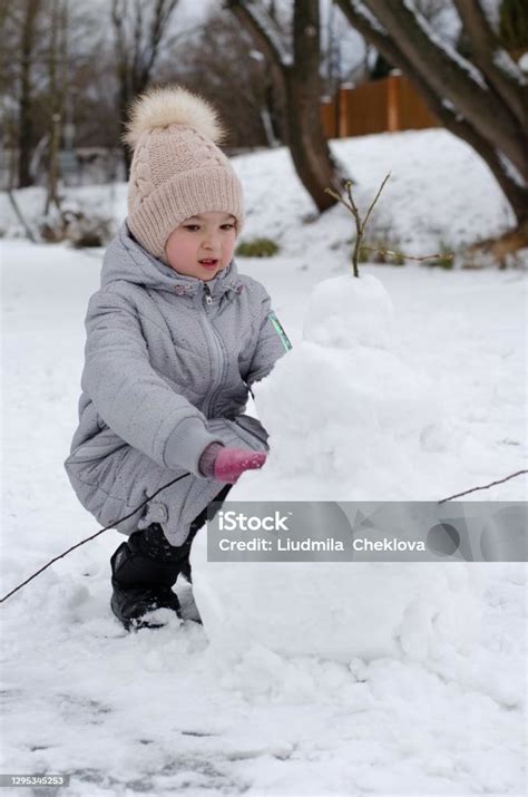 겨울 옷을 입은 소녀와 겨울 공원에서 눈으로 노는 모자 어린이는 겨울 방학 동안 밖에 있습니다 한 어린이가 눈덮인 눈사람을 만든다 6 7 살에 대한 스톡 사진 및 기타