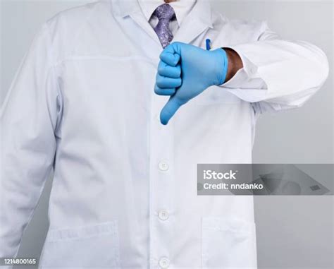 버튼이달린 흰색 코트를 입은 의사가 파란색 의료 용 장갑을 착용하고 손으로 싫어하는 제스처를 보여줍니다 싫어요 버튼에 대한 스톡