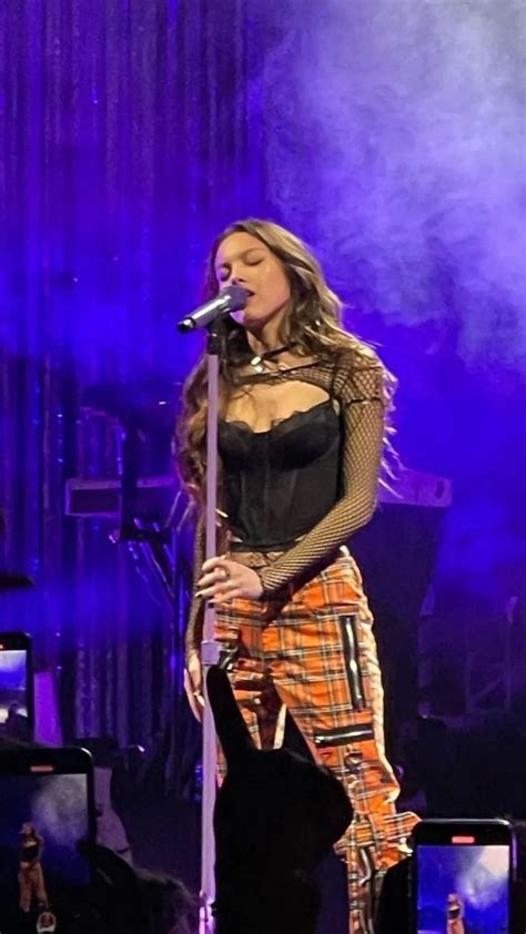 A Woman Standing On Top Of A Stage With A Microphone In Her Hand And Wearing Plaid Pants