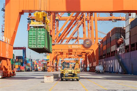 트럭이 컨테이너에 적재되어 항구 터미널과 부두 크레인을 배경에 서있을 준비가되고 있습니다 항구 운영 활동 컨테이너 운송 및 물류에 대한 보기 2025년에 대한 스톡 사진 및