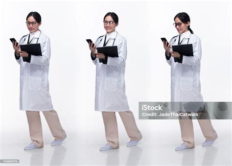 청진기를 든 전체 길이 30대 40대 아시아 여성 의사 왼쪽 오른쪽으로 앞으로 걷고 공식적인 코트 바지 신발을 신습니다 미소 병원 여성 캐리 환자 차트 전화 흰색 배경 위에