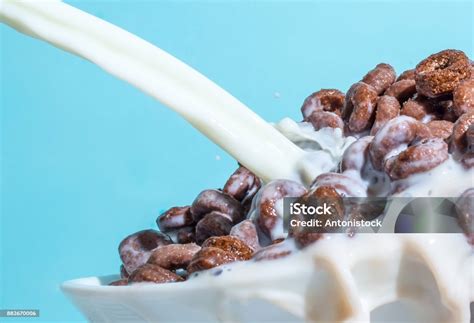 Сornflakes 근접 그릇에 붓는 우유 스트림 컵에 우유 스플래시 파란색 배경에 조각 매크로 곡초류에 대한 스톡 사진 및