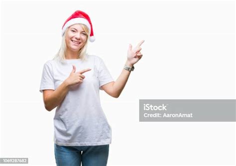 젊은 아름 다운 금발 여자 웃 고 옆에 두 손과 손가락으로 가리키는 카메라 보고 격리 된 배경 위에 크리스마스 모자를 쓰고 가리키기에 대한 스톡 사진 및 기타 이미지
