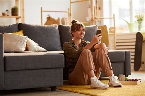 스낵을 하는 동안 카펫에 앉아 서 게시물을 읽고 머리 롤빵과 미소 아름 다운 젊은 여자 가정 생활에 대한 스톡 사진 및 기타 이미지 가정 생활 고객 참여 기업가