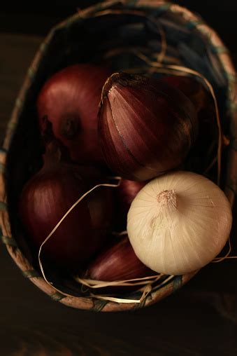 빨간색 스페인 양파의 여러 머리와 고리 버들 바구니에 접힌 한 흰색 어두운 갈색 배경입니다 식품 저장 요리 준비 평면도 마을의