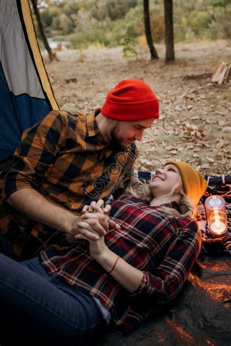 밝은 니트 모자를 쓴 젊은 커플이 화재 옆 캠프장에서 잠시 멈춥니다 Photo 사진 무료 다운로드 Lovepik