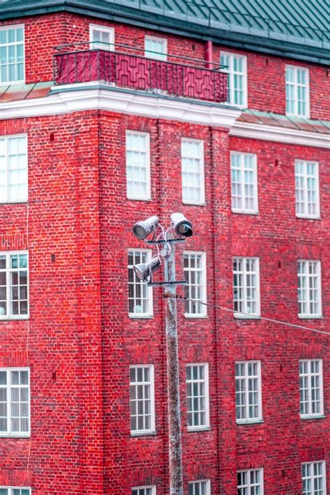 Urban Surveillance Cameras In Front Of A Red Brick Building With Multiple Windows Providing