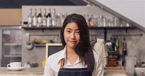 젊은 아시아 여성 바리스타가 음료 바 카운터를 배경으로 커피숍에 오신 고객을 환영하기 위해 웃고 있는 모습 젊은 여성 바리스타가 커피숍에서 미소를 짓고 있다 음식과 음료