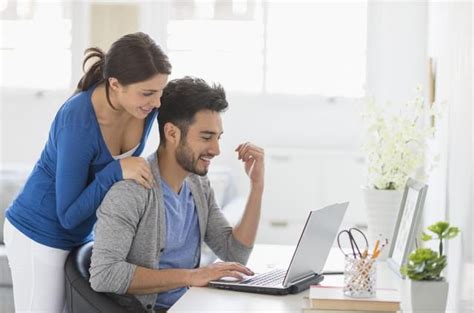 A Man And Woman Sitting At A Table With A Laptop