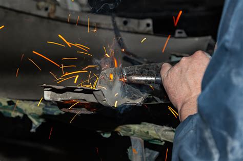 클로즈업 보기 강한 남자는 팔에 장갑 없이 파란색 작업 바지에 용접기 금속 제품은 차고 워크샵에서 용접 기계로 용접 블루 연기와 오렌지 스파크 멀리 날아 강철에 대한 스톡